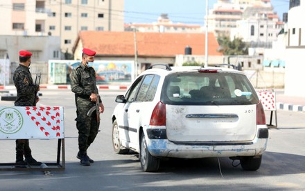 Palestinian policemen wear face masks, guard a barrier blocking a road ...