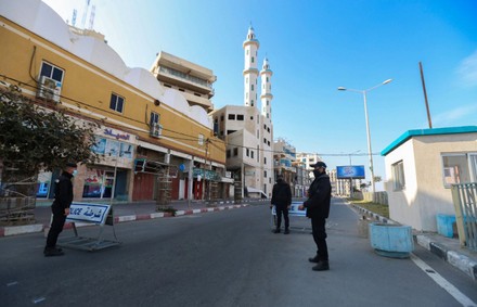 Palestinian policemen wear face masks, guard a barrier blocking a road ...