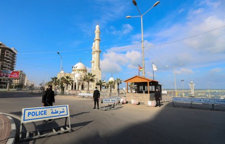 Palestinian policemen wear face masks, guard a barrier blocking a road ...